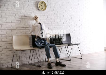 Human skeleton in office wear sitting on chair near brick wall indoors ...