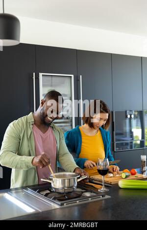 Vertical of happy diverse couple cooking together and using tablet in ...