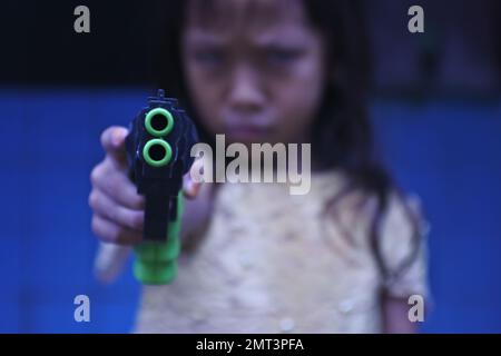 A sad girl pointing a toy gun on the camera in a selective focus Stock ...