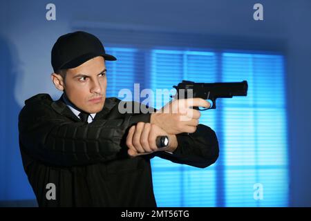 Professional security guard with gun and flashlight checking dark room ...
