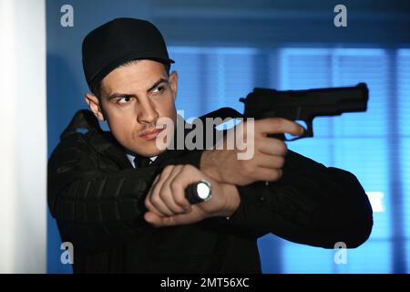 Professional security guard with gun and flashlight checking dark room ...