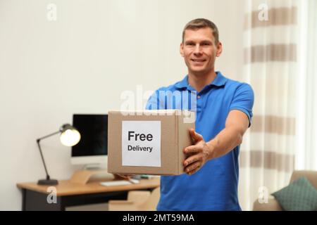 Courier holding parcel with sticker Free Delivery indoors, closeup ...