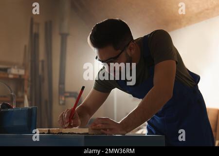 Professional carpenter making mark on wooden bar in workshop, closeup ...