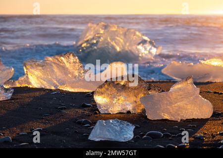 Pure Ice Shining on Black Volcanic Sand at Sunset, Ocean Waves Crash ...