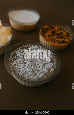 A vertical shot of plastic bowls of various creamy pudding on a brown ...