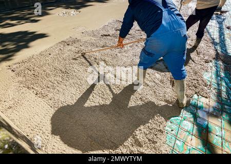 Construction worker, rigger is using rake to spreading, leveling ...