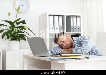 Lazy young man wasting time at table in office Stock Photo - Alamy