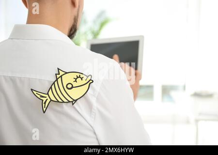 Man with paper fish on back against blue background. April fool's day ...