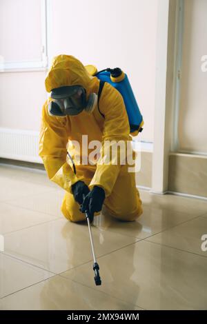 Pest control worker in protective suit spraying insecticide on window ...