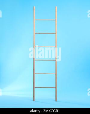 Modern wooden ladder on light blue background Stock Photo - Alamy