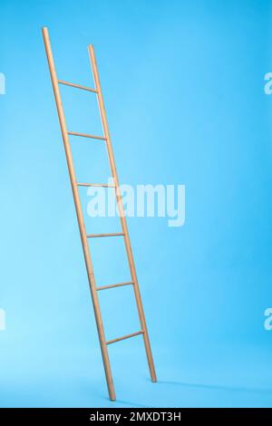 Modern wooden ladder on light blue background Stock Photo - Alamy