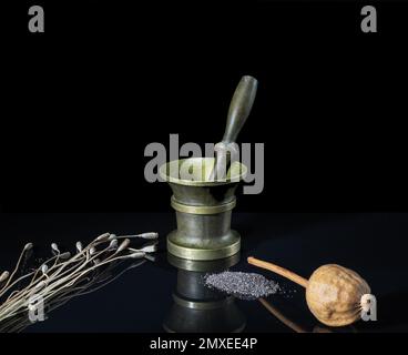 a bronze poppy mortar and poppy stalks are reflected in a black mirror ...