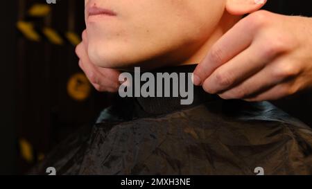 Hairdresser putting on special paper collar on neck of his client ...