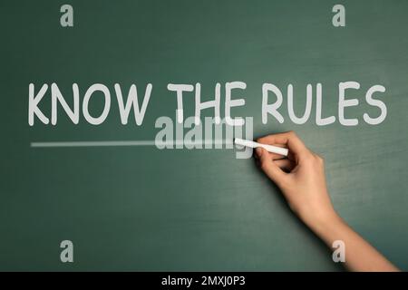 Woman underlining phrase Know the rules on green chalkboard, closeup ...