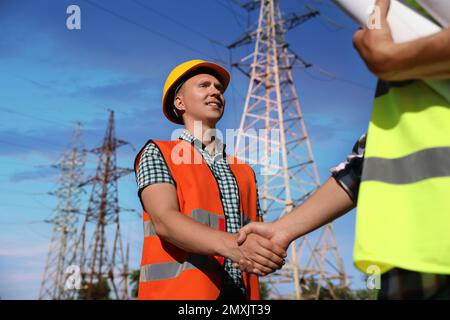 Professional electricians shaking hands near high voltage tower ...