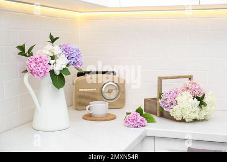 Beautiful hydrangea flowers, cup and radio set on light countertop ...