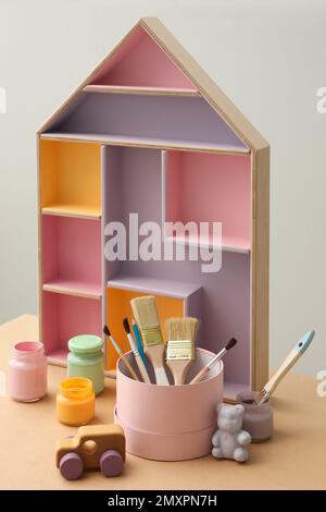 Composition with house shaped shelf and jars of paints on table ...