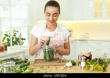 Woman putting cucumber into pickling jar at table in kitchen Stock ...