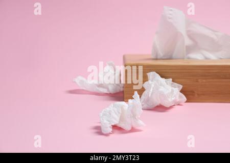 Holder with paper tissues and used crumpled napkins on pink background ...