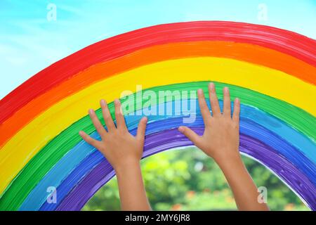 Child touching picture of rainbow on window, closeup. Stay at home ...