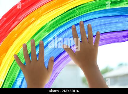 Child touching picture of rainbow on window, closeup. Stay at home ...