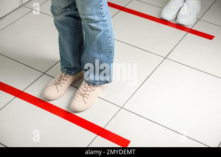 People standing in line behind taped floor markings for social distance ...