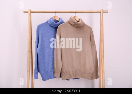 Rack with knitted sweaters near blue wall Stock Photo - Alamy