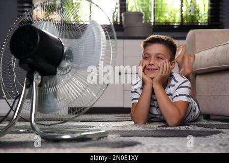 Little boy enjoying air flow from portable fan on white background ...