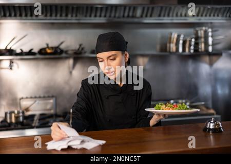 Female chef checks the prepared dish with the paid check in kitchen of ...