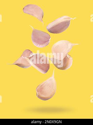 Many garlic cloves falling on yellow background Stock Photo - Alamy