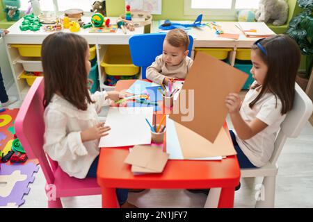 Adorable caucasian boy student cutting paper sitting on table at ...