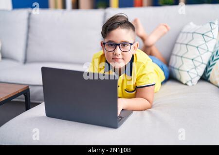 Adorable hispanic boy using laptop and headphones sitting on sofa at ...