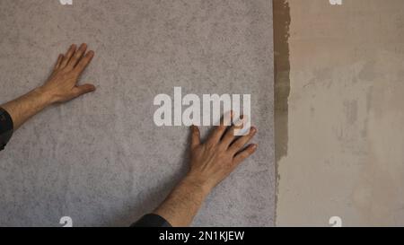 man pasting a strip of gray wallpaper on the room wall next to the ...