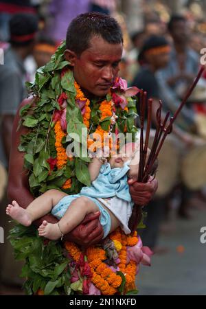 A Hindu priest, face smeared with color and sacrificial blood, carries ...