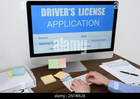 Man using computer to fill driver's license application form at table in office, closeup Stock ...