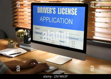 Woman using computer to fill driver's license application form at table ...