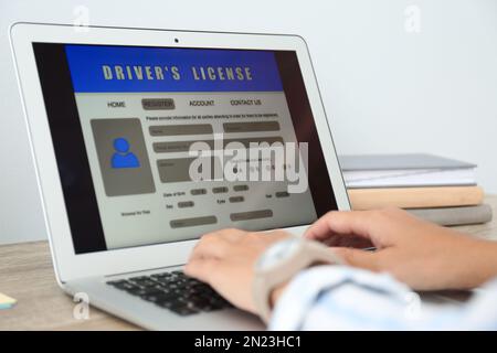 Woman using laptop to fill driver's license application form at table in office, closeup Stock ...
