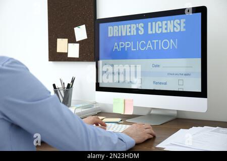 Man using computer to fill driver's license application form at table in office, closeup Stock ...