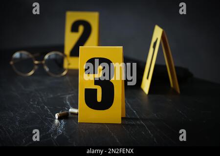Shell casings and evidence marker on black slate table, closeup. Crime ...