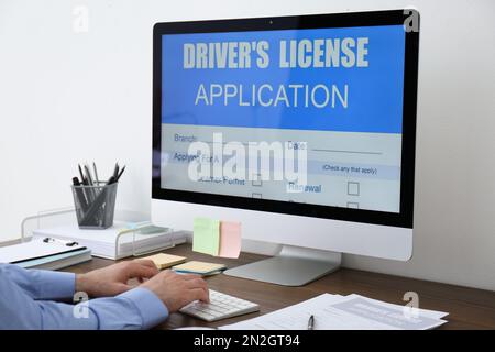 Man using computer to fill driver's license application form at table in office, closeup Stock ...