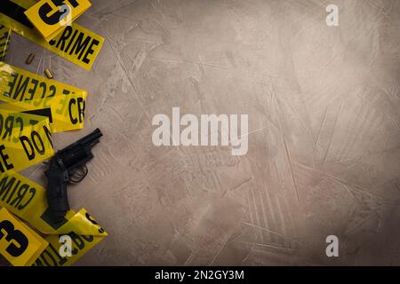 Flat lay with yellow tape, crime scene marker and gun on grey stone ...