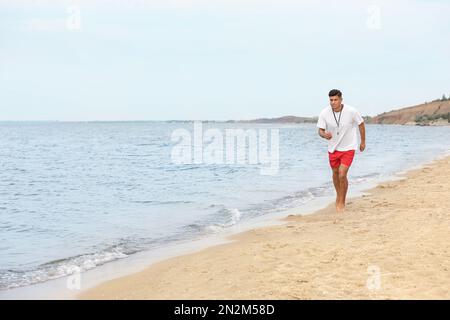 Handsome male lifeguard running on sandy beach Stock Photo - Alamy