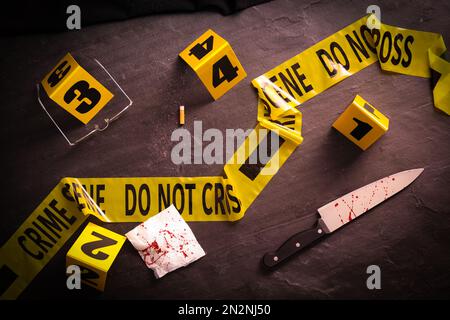 Flat lay composition with evidences and crime scene tape on black slate ...