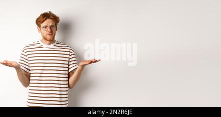 Confused boyfriend with red hair shrugging, spread hands sideways and ...