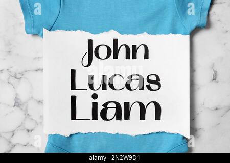 Bodysuit with different baby names on white marble background, top view ...