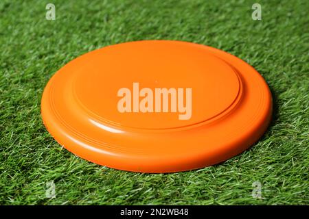 Orange plastic frisbee disk on green grass, top view. Space for text ...