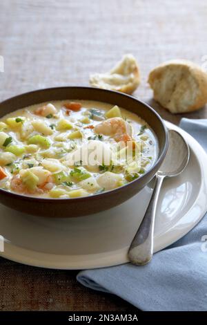 Bowl of seafood chowder with crusty bread on a grey table with a green ...