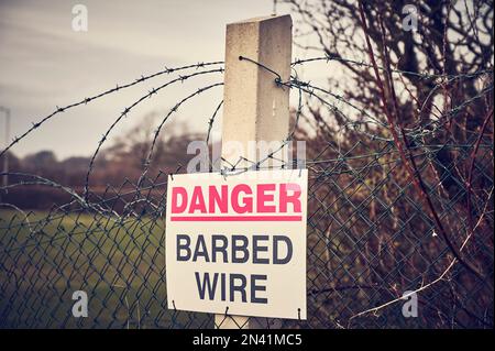 Sign warning of barbed wire attached to wire fence Stock Photo - Alamy