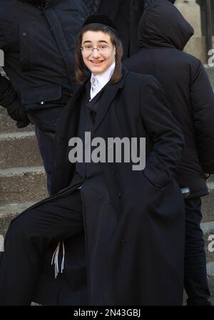 Posed portrait of a hasidic boy with long peyot and a smile. In ...