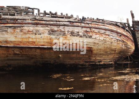 The hull of a long wooden ship leaning to one side, decaying and ...